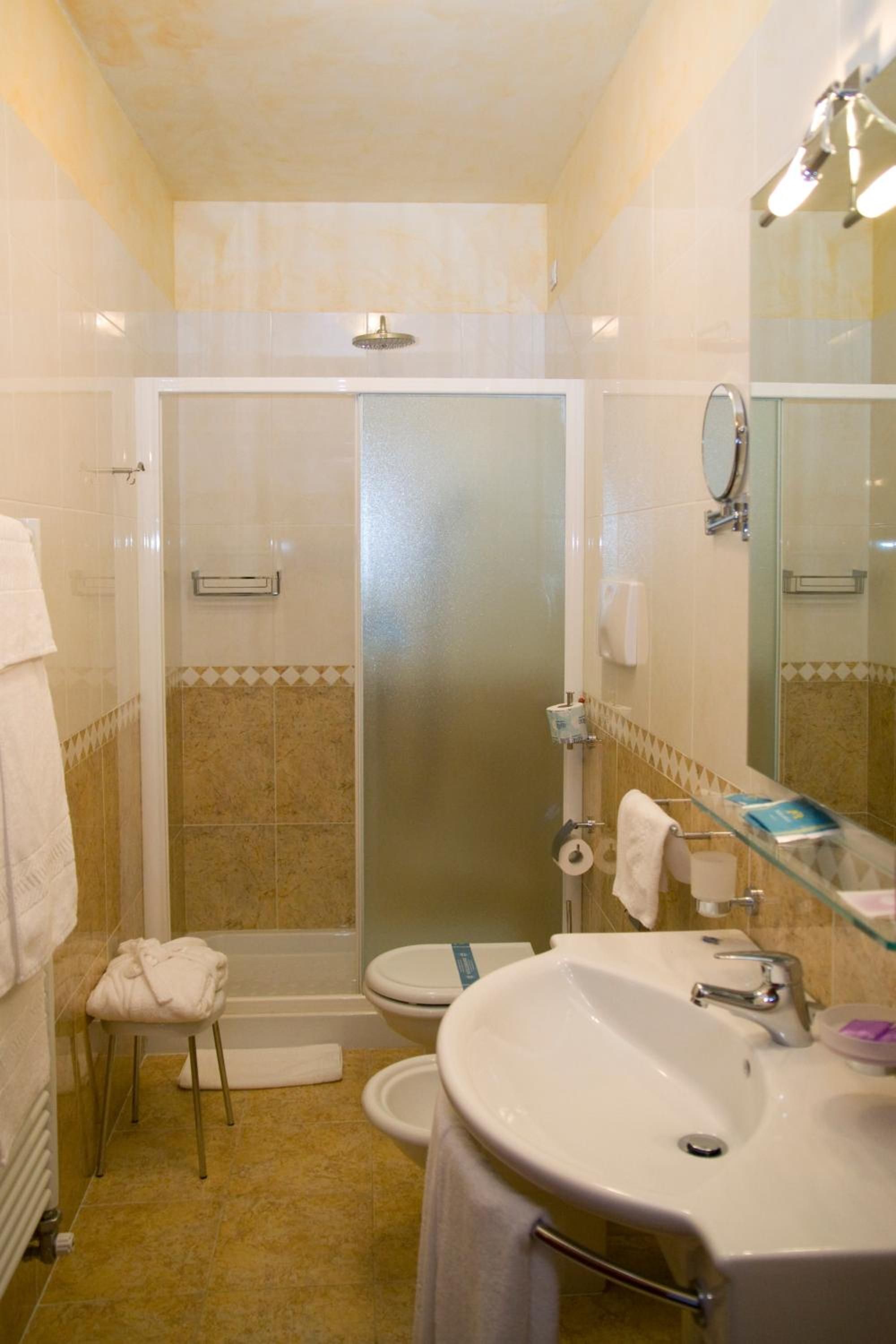 Casa de banho com chuveiro em cabine de vidro, sanita, lavatório com espelho e porta-toalhas.