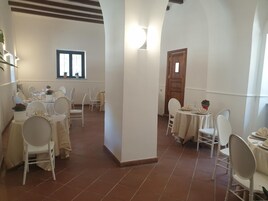 Uma sala de jantar com cadeiras e mesas brancas, uma porta de madeira e uma janela com persianas.