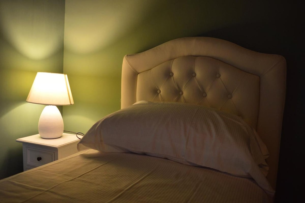 Uma cama com cabeceira estofada, abajur e travesseiro.