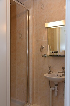 Casa de banho com cabine de duche em vidro, lavatório com espelho e prateleira com produtos de higiene pessoal.