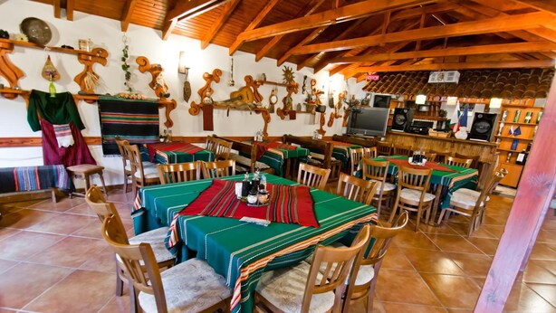 Um restaurante com mesas e cadeiras de madeira, cobertas por toalhas de mesa coloridas.