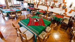 Restaurante com várias mesas e cadeiras, cada uma coberta por toalha de mesa verde e um corredor de mesa listrado em vermelho e branco.