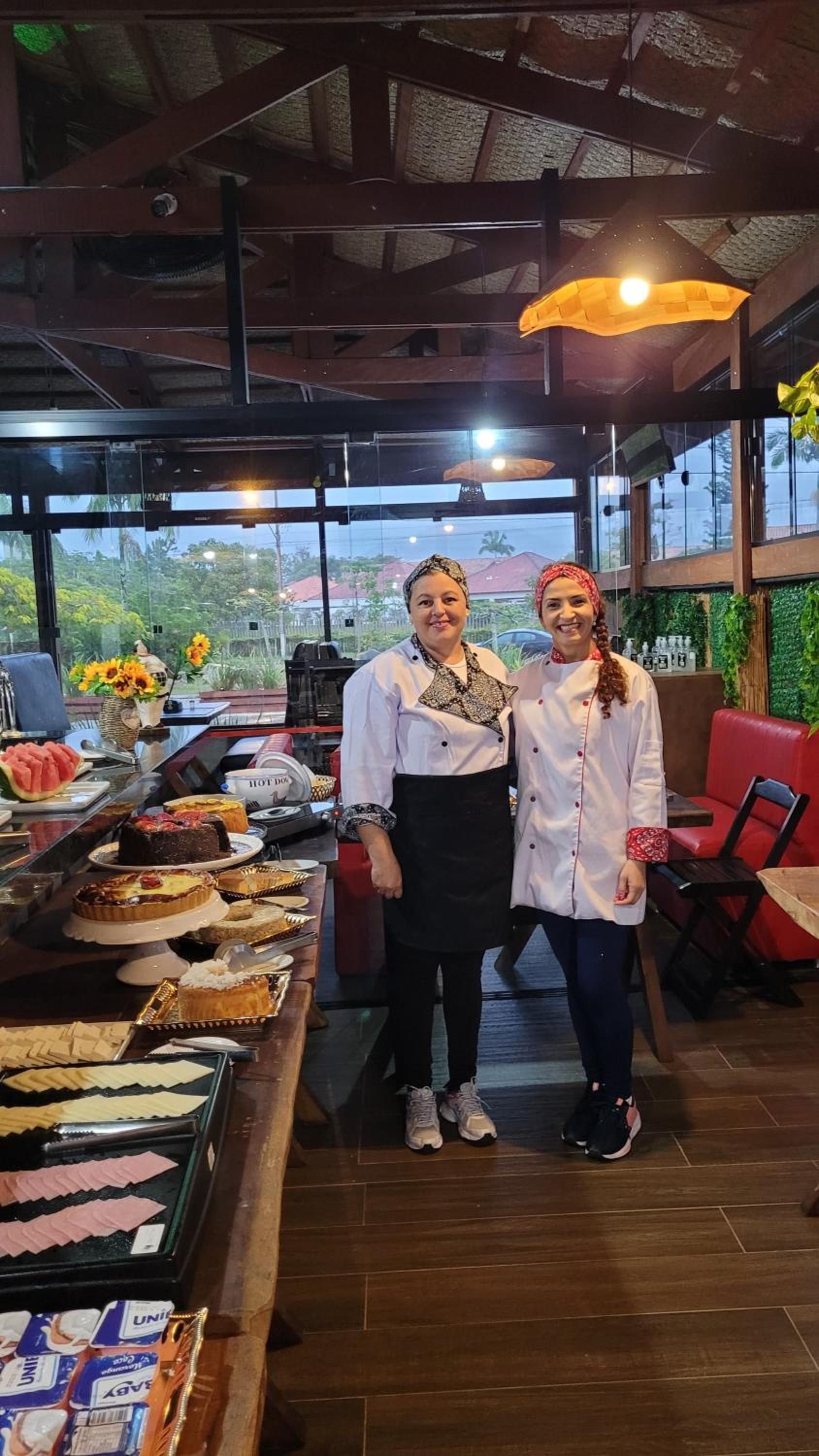 Duas pessoas em um restaurante, com diversas sobremesas expostas.