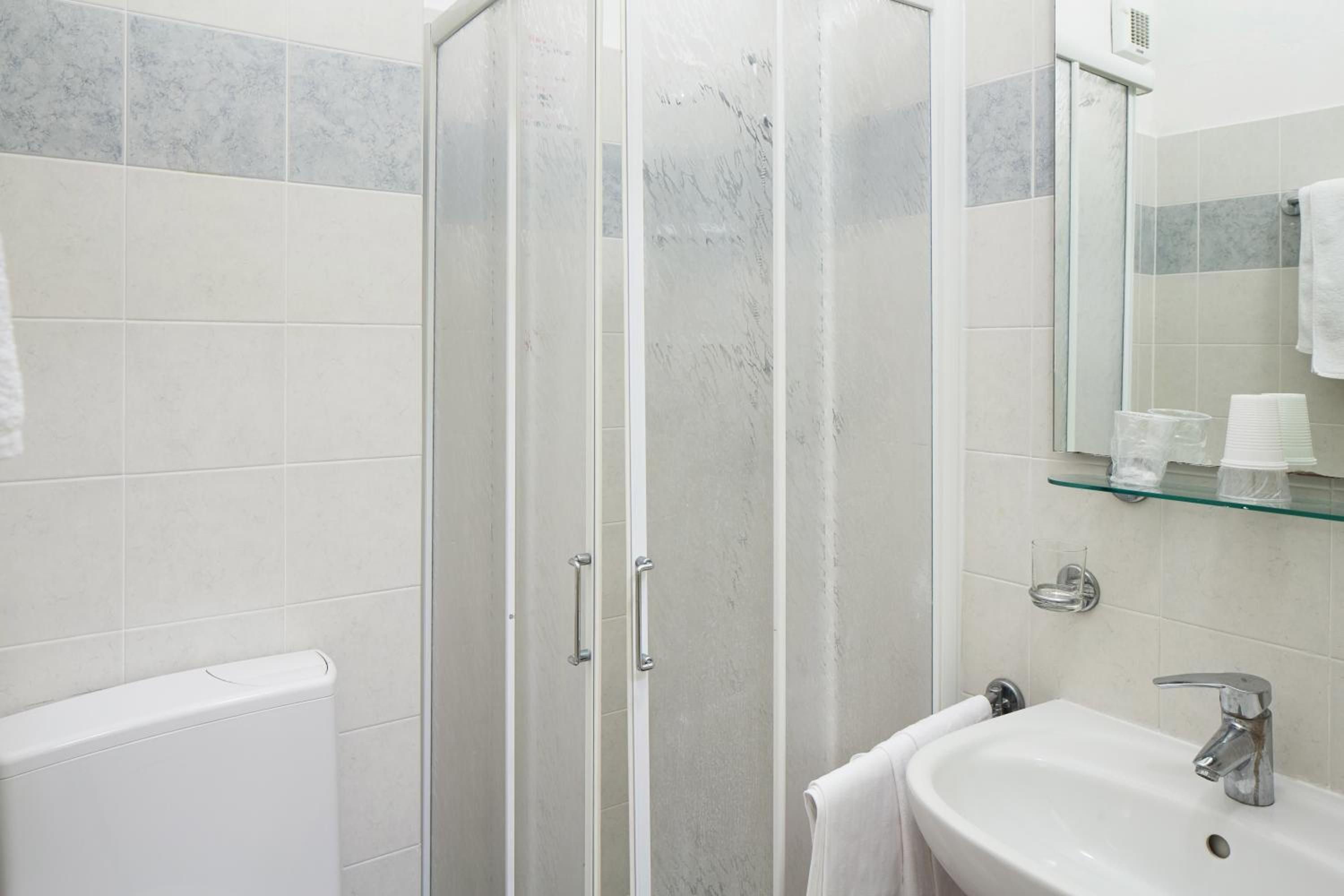 Casa de banho com chuveiro em cabine de vidro, lavatório branco e prateleira de vidro com produtos de higiene pessoal.