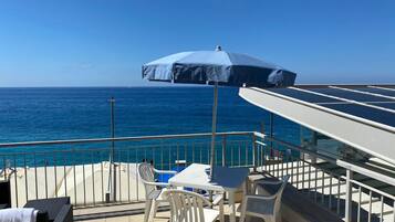 Terraço com mesa e cadeiras, vista para uma piscina e o mar.