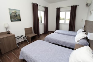 Quarto de hotel com duas camas, uma mesa de escritório, uma cadeira, uma mesinha de centro e uma janela com cortinas.