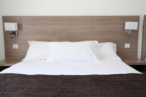 Cama com lençóis brancos e um cobertor marrom, com duas mesas de cabeceira e luminárias de cada lado.