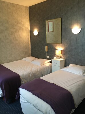 Quarto de hotel com duas camas, uma mesa de cabeceira com abajur e telefone fixado na parede.