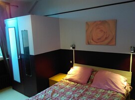 Quarto com cama, mesa de cabeceira, luminária na parede e uma porta.