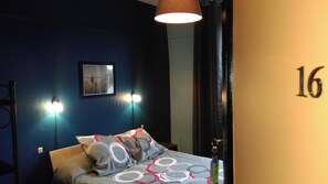 Quarto de hotel com uma cama, um quadro na parede e o número '16' na parede.