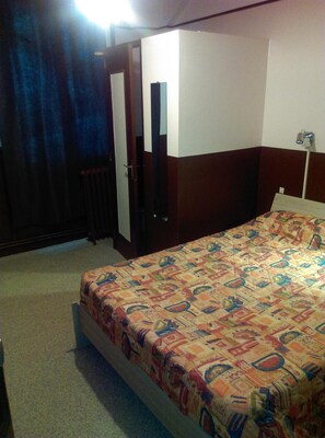 Quarto com cama, porta, radiador e luminária fixada na parede.