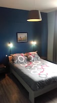 Quarto com cama, duas luminárias de cabeceira, um quadro na parede e uma janela.