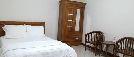 Quarto com cama, guarda-roupa de madeira e duas cadeiras de madeira.