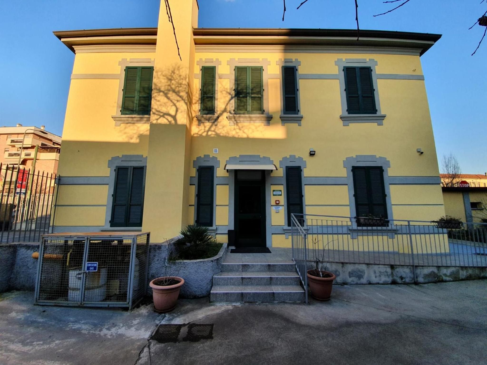 Um edifício amarelo com porta frontal, janelas com persianas e pequena entrada com degraus.