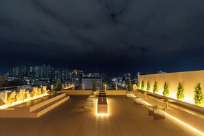 Terraço no telhado com vista para o horizonte urbano, apresentando design moderno com formas geométricas e diversos vasos de plantas.