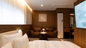 Quarto de hotel com cama, área de estar com mesa, televisão e porta para o banheiro.