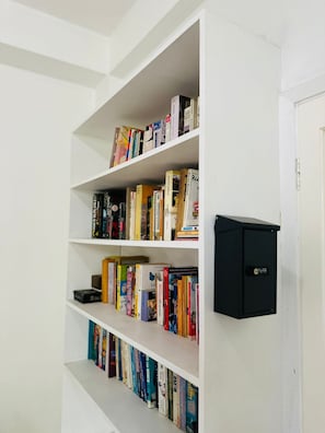 Uma estante com vários livros e um dispositivo eletrônico preto na parede.