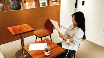 Uma mulher sentada à mesa de madeira, lendo um documento com uma bebida.