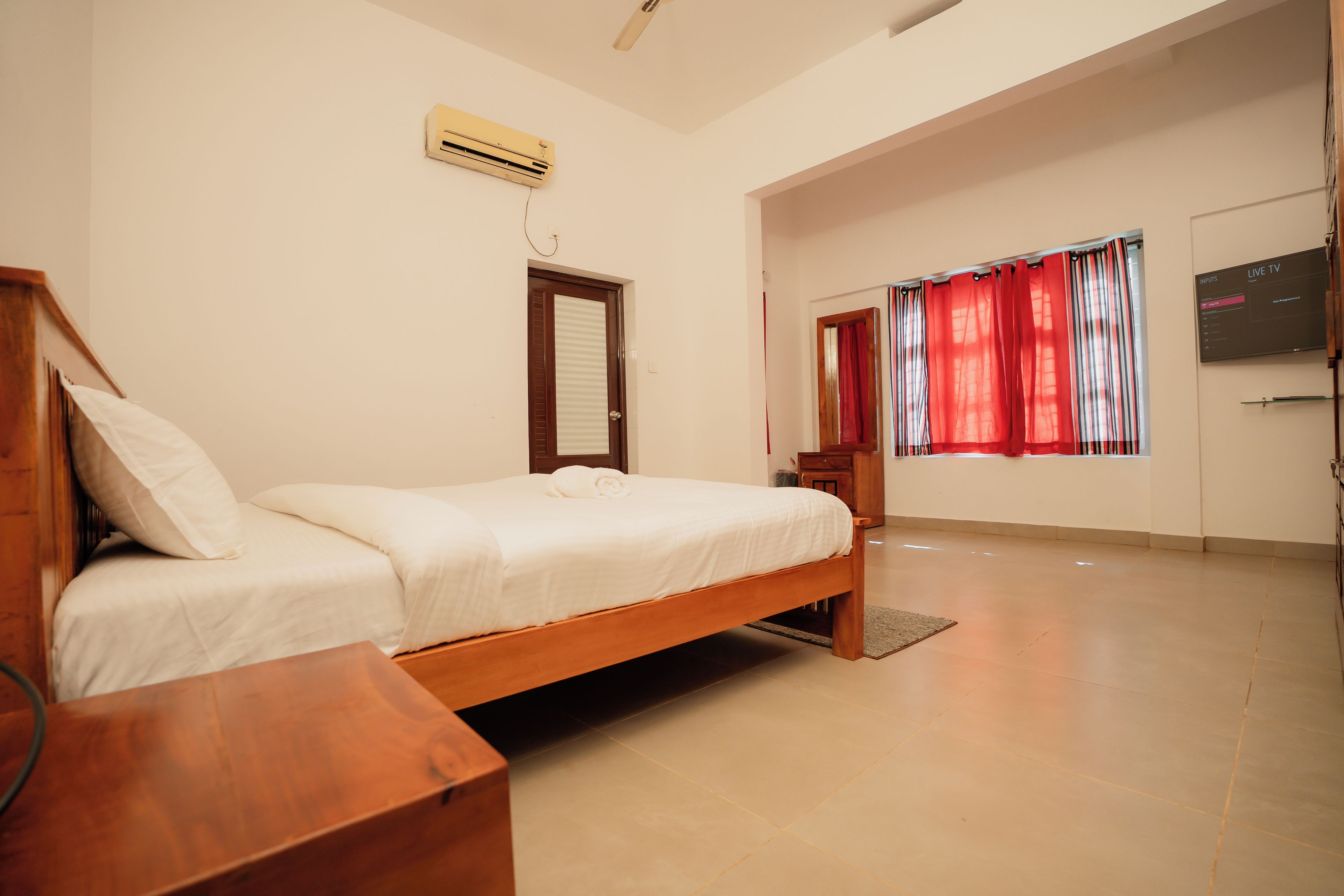 Quarto com cama, mesa de cabeceira de madeira, guarda-roupa, televisão e janela com cortinas.