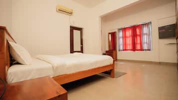 Quarto com cama, mesa de cabeceira de madeira, guarda-roupa, televisão e janela com cortinas.