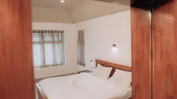 Quarto com cama de madeira, roupa de cama branca, mesa de cabeceira, luminária na parede e janela com cortinas.