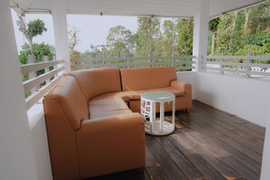Sofá modular bege e mesa redonda branca sobre um deck de madeira com guarda-corpos brancos.