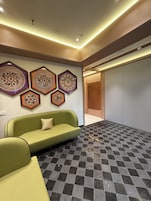 Um hall com sofá verde, decorações de parede estampadas e piso xadrez.