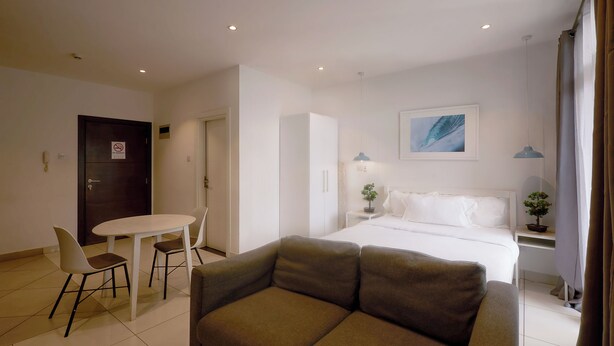 Quarto de hotel com cama, sofá, mesa de jantar com cadeiras, pequena escrivaninha e porta com placa.