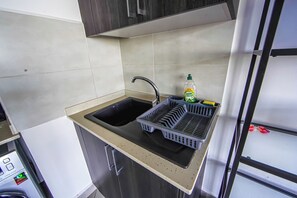 Cozinha compacta com pia, escorredor de louça e uma garrafa de detergente.