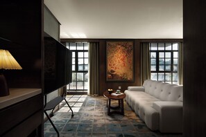 Quarto de hotel com sofá, televisão, pintura e vista pelas janelas.