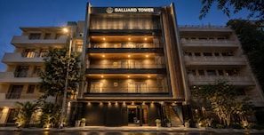 Um hotel com vários andares chamado 'GALLIARD TOWER', com design moderno, com varandas e uma entrada bem iluminada.