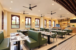 Restaurante com assentos e mesas verdes, ventiladores de teto e piso de azulejos.