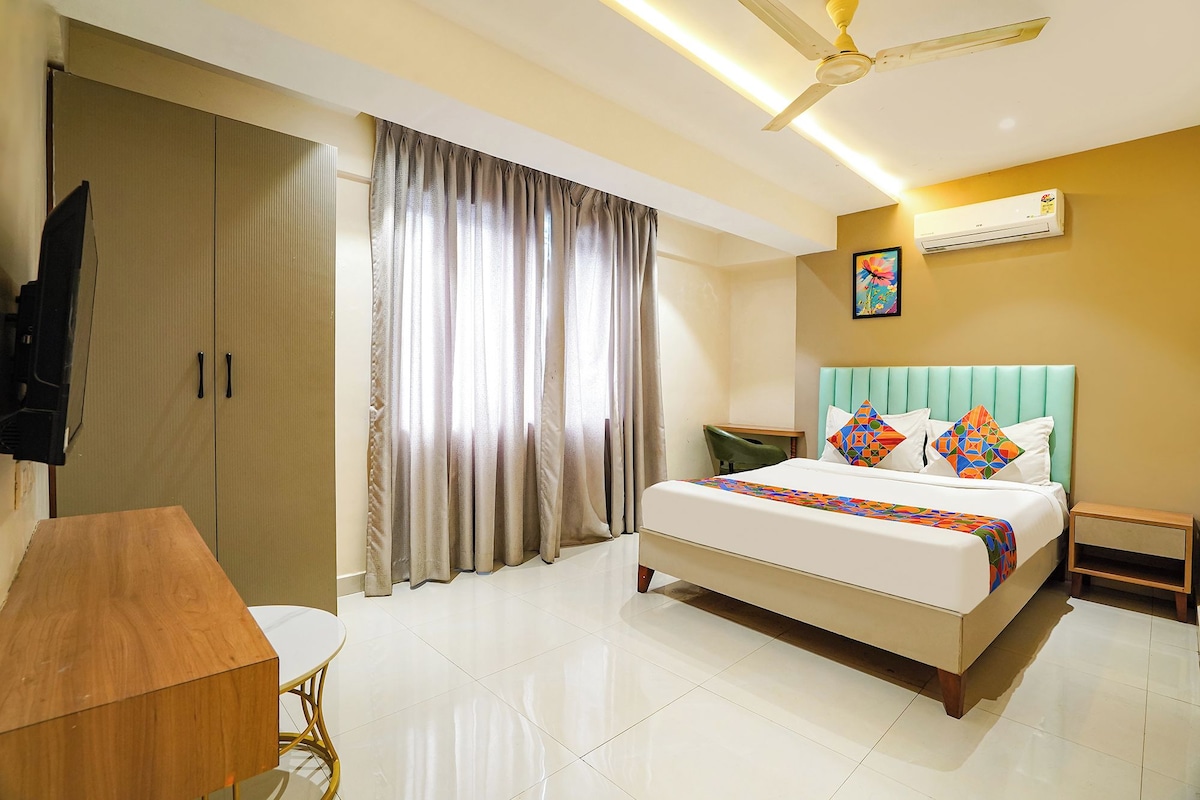 Quarto de hotel com cama, escrivaninha, cadeira, guarda-roupa, ventoinha no teto e ar condicionado.