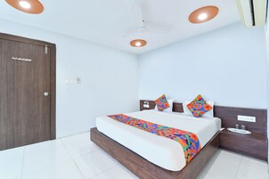Quarto com cama, mesa de cabeceira, ventoinha no teto e porta.