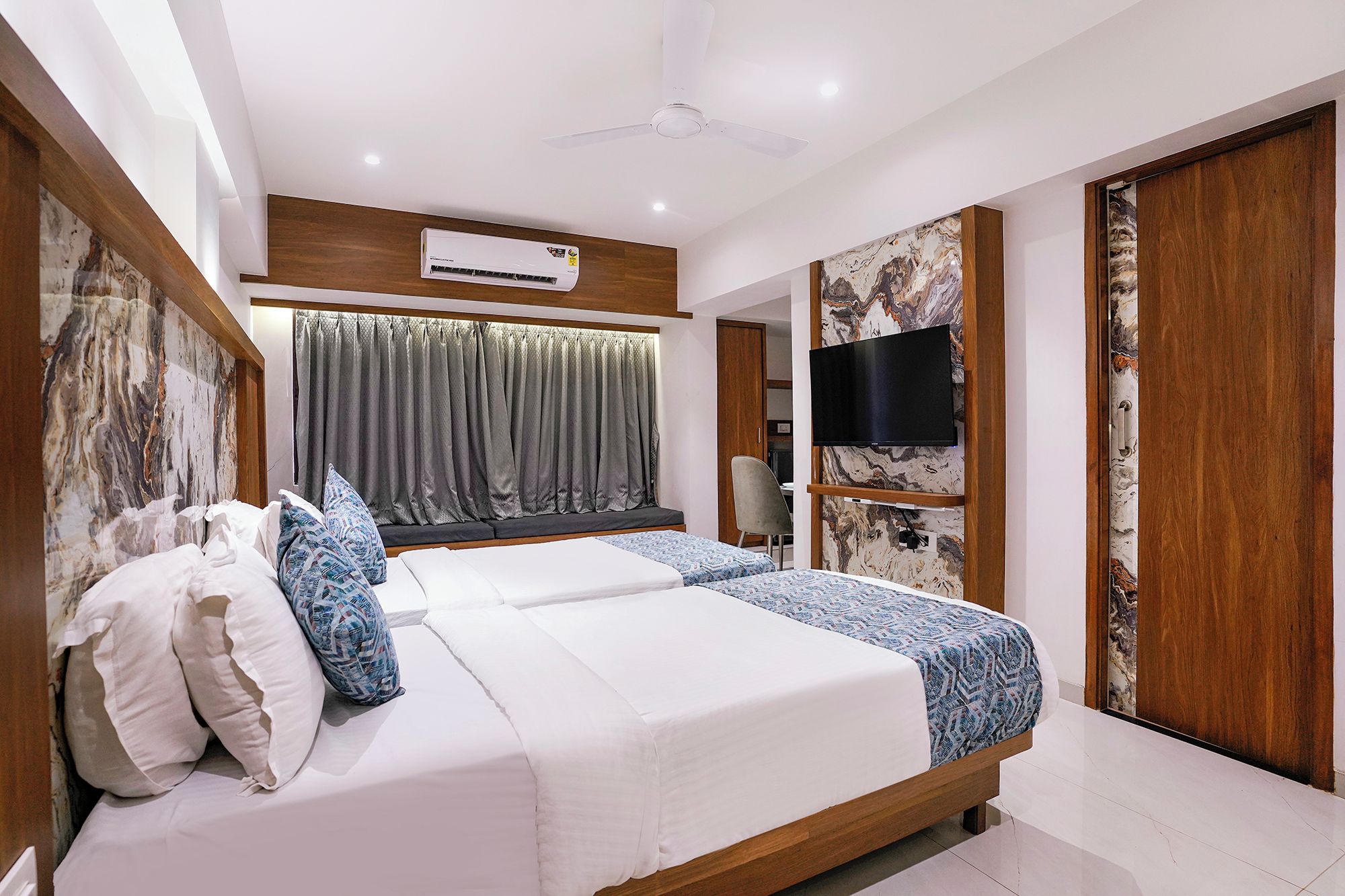 Quarto de hotel com cama, televisão, ventoinha no teto e guarda-roupa.