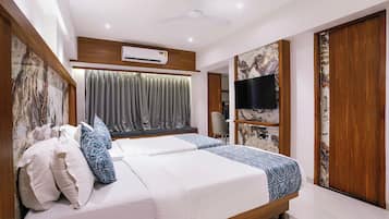 Quarto de hotel com cama, televisão, ventoinha no teto e guarda-roupa.