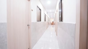 Um corredor com portas em ambos os lados, piso ladrilhado e teto com iluminação embutida.