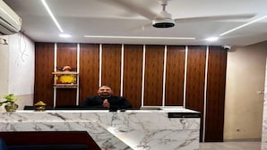 Balcão de recepção com tampo de mármore, ventilador de teto e painel de parede em madeira.