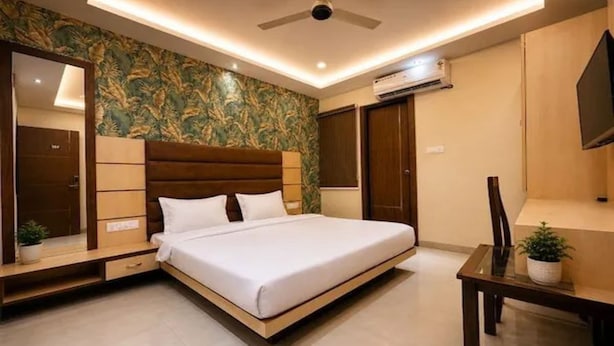 Quarto moderno com cama, mesas de cabeceira, espelho, ventoinha no teto e ar condicionado, além de uma TV.