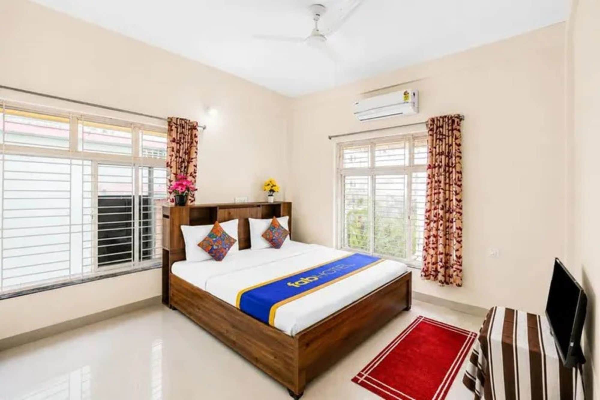 Quarto de hotel com cama, televisão, janela com cortinas e aparelho de ar condicionado.