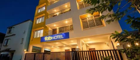 Hotel de vários andares com uma placa chamativa, varandas e entrada protegida por portão.