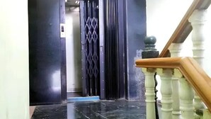 Um corredor com porta preta, piso de mármore e corrimão de madeira.