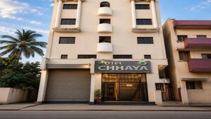 Um hotel chamado 'HOTEL CHHAYA' com a porta da frente fechada, uma varanda no segundo andar e uma palmeira ao fundo.