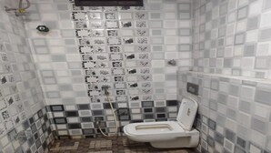 Um banheiro pequeno com vaso sanitário, chuveiro e parede revestida de azulejos.