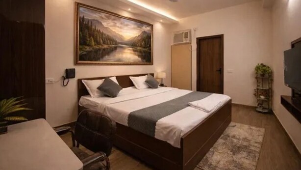 Quarto com cama, mesa de cabeceira, abajur e um quadro na parede.