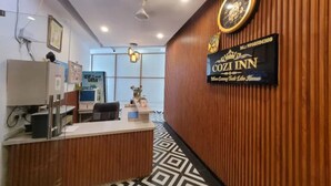 Uma área de recepção com balcão de madeira, um relógio e um letreiro indicando 'Cozzi Inn'.