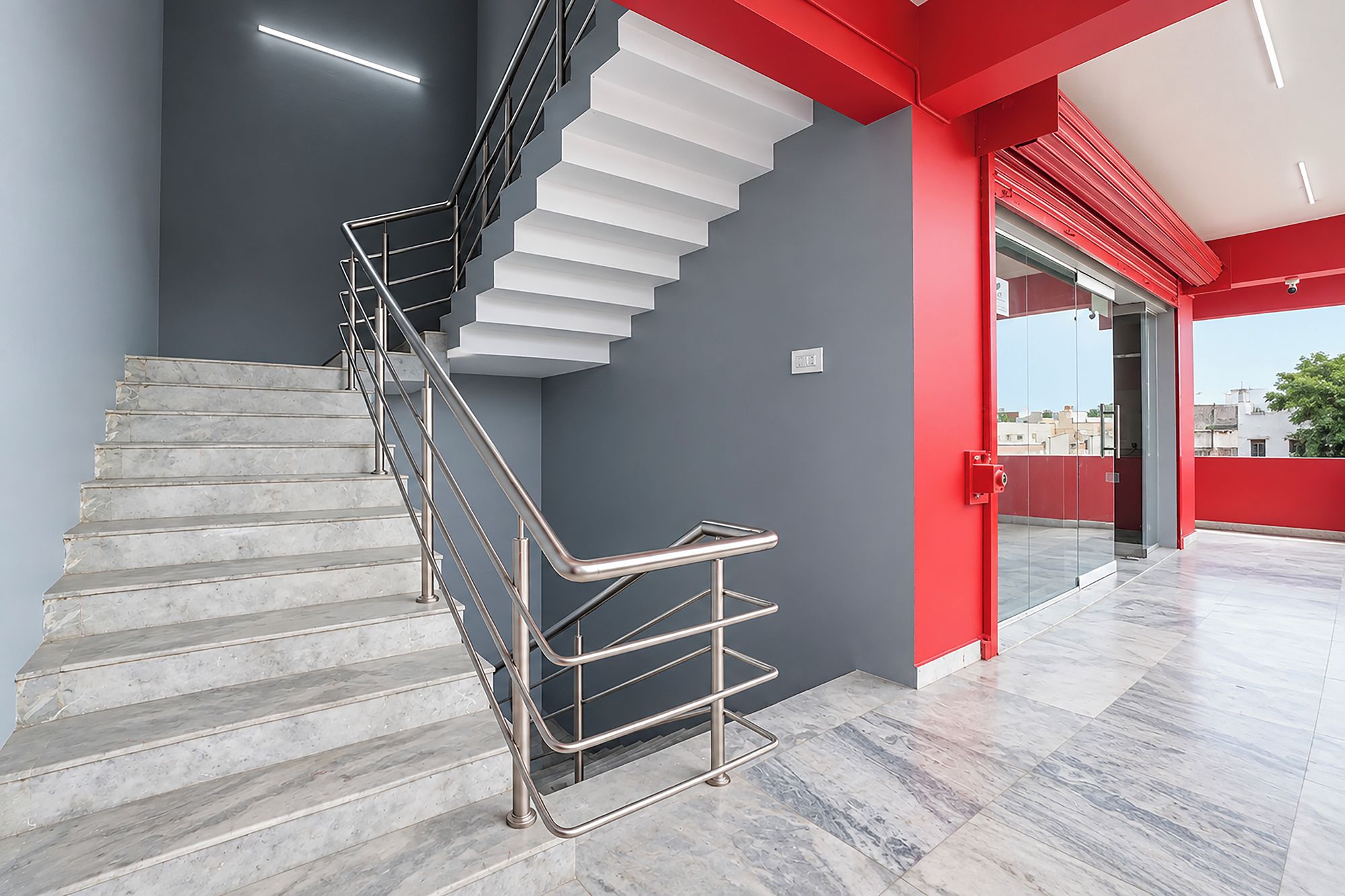 Uma escadaria moderna com corrimãos de metal, uma parede cinza e uma parede com destaque em vermelho.