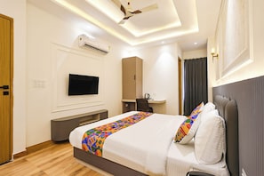 Quarto de hotel com cama, TV de tela plana, escrivaninha, cadeira, cafeteira e ventilador de teto.