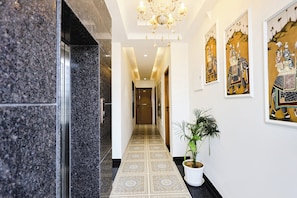 Um corredor com piso de mármore, planta em vaso e quadros nas paredes.