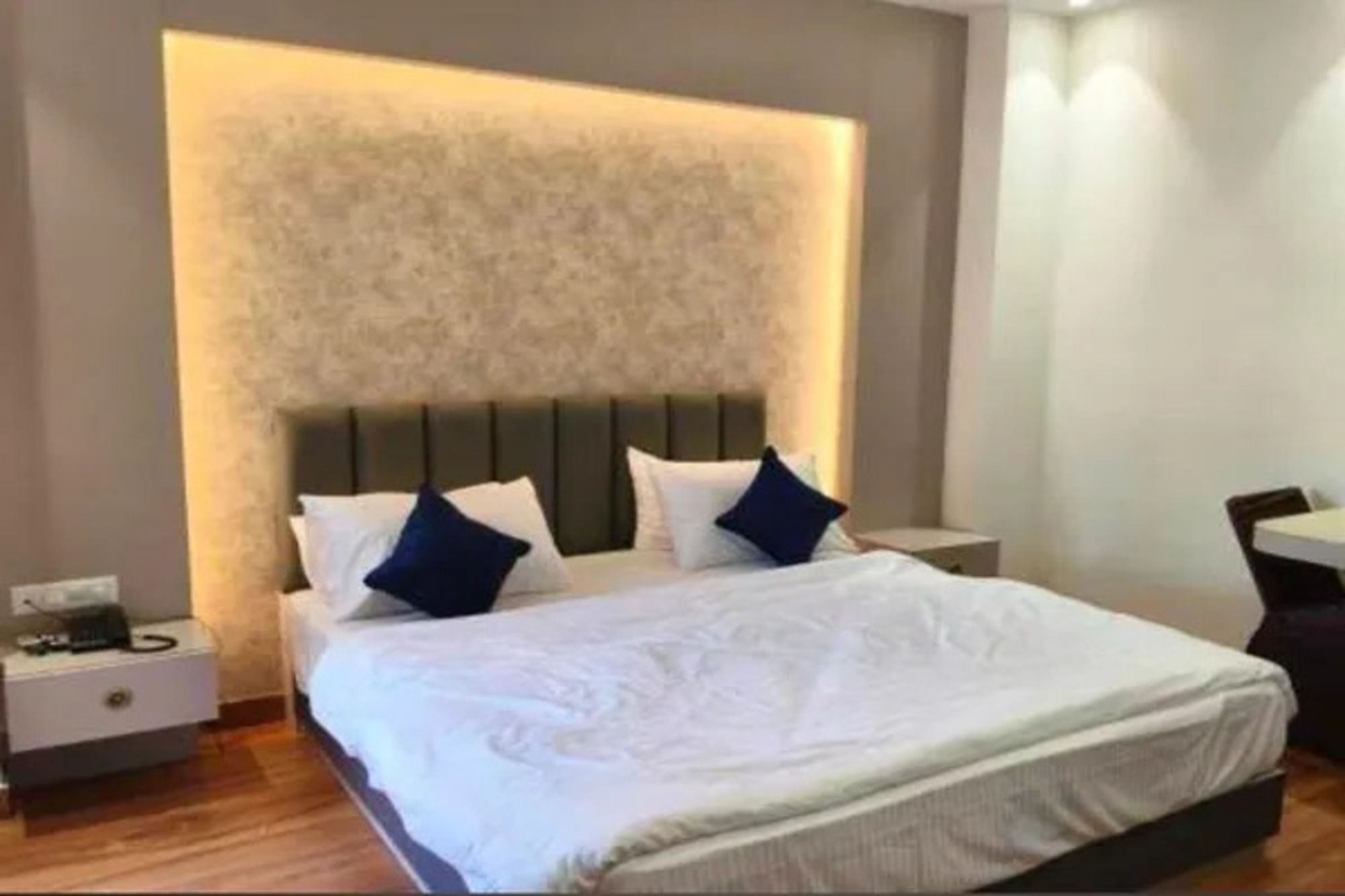 Quarto de hotel com uma cama grande, cabeceira com iluminação embutida e mesa de cabeceira com telefone.